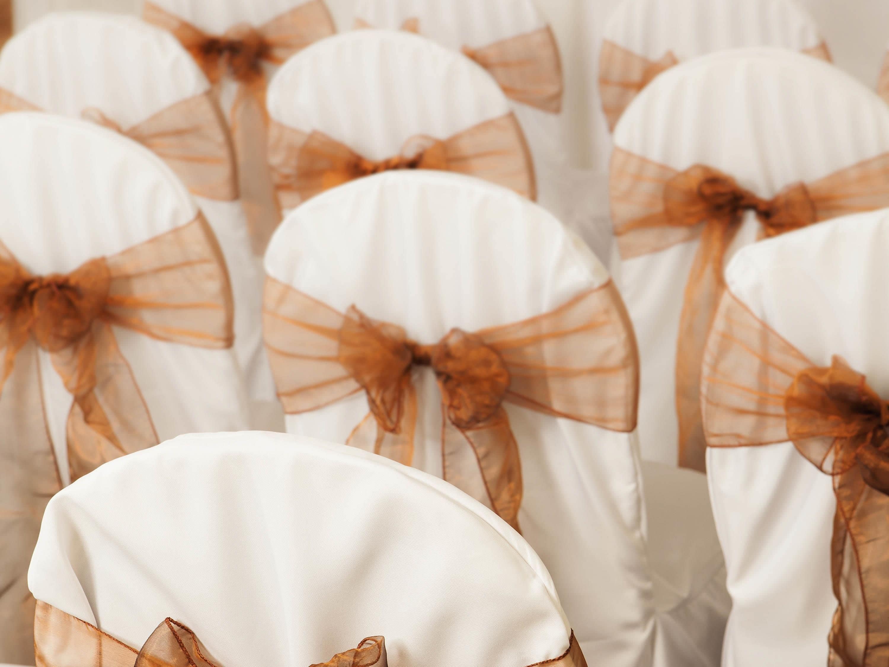 Fileiras de cadeiras com capas brancas e laços marrons.