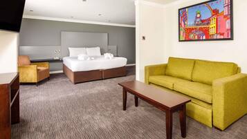 Quarto de hotel com uma cama, um sofá verde, uma mesa de madeira e um quadro na parede.