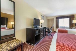 Quarto de hotel com duas camas, uma mesa com computador, televisão e espelho.