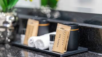 Uma bandeja com uma toalha enrolada, uma caneca preta e um saco de papel marrom com a etiqueta 'Vanity Kit' sobre uma bancada preta.