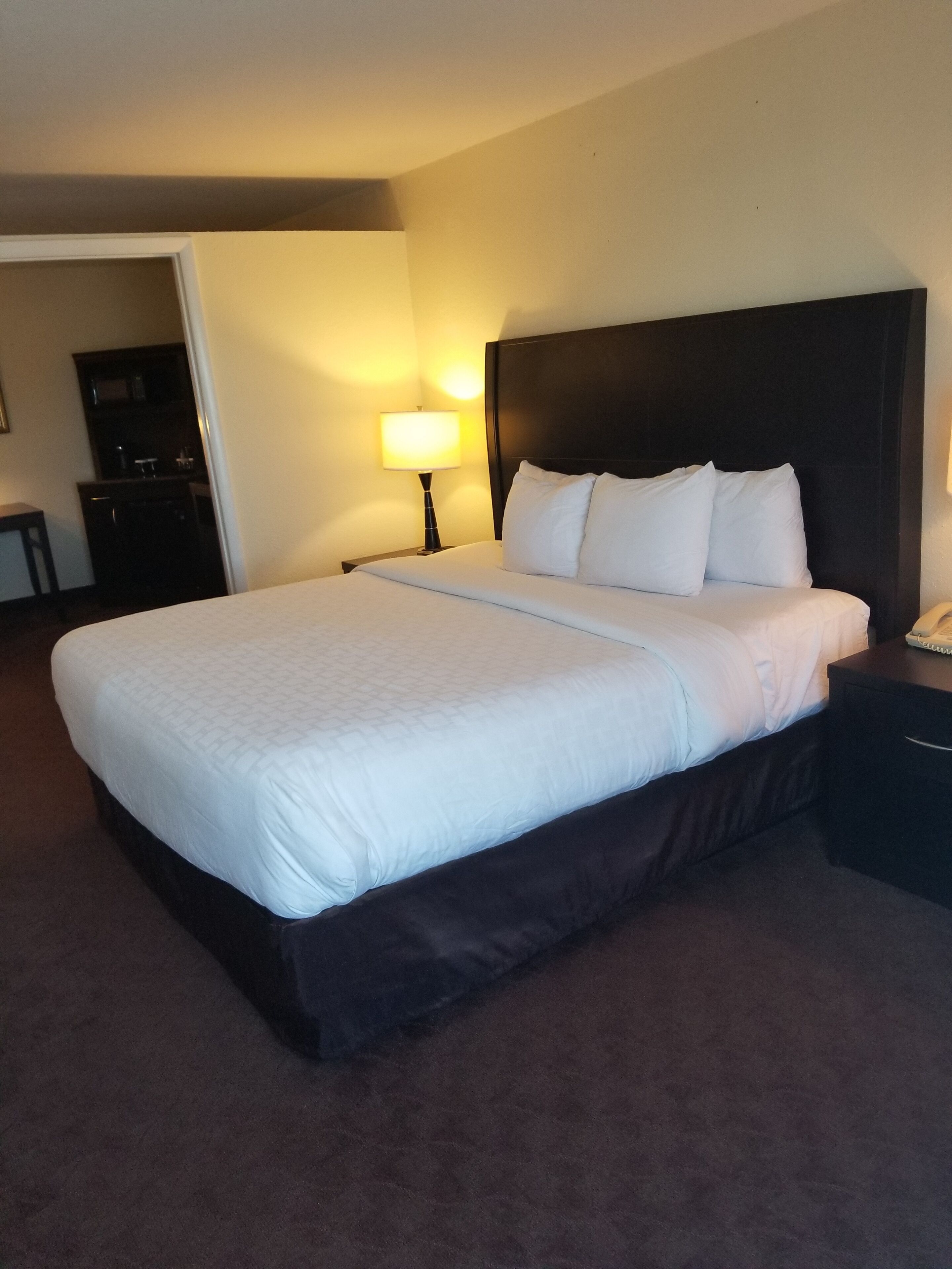 Quarto de hotel com uma cama grande, mesa de cabeceira, abajur e escrivaninha com cadeira.