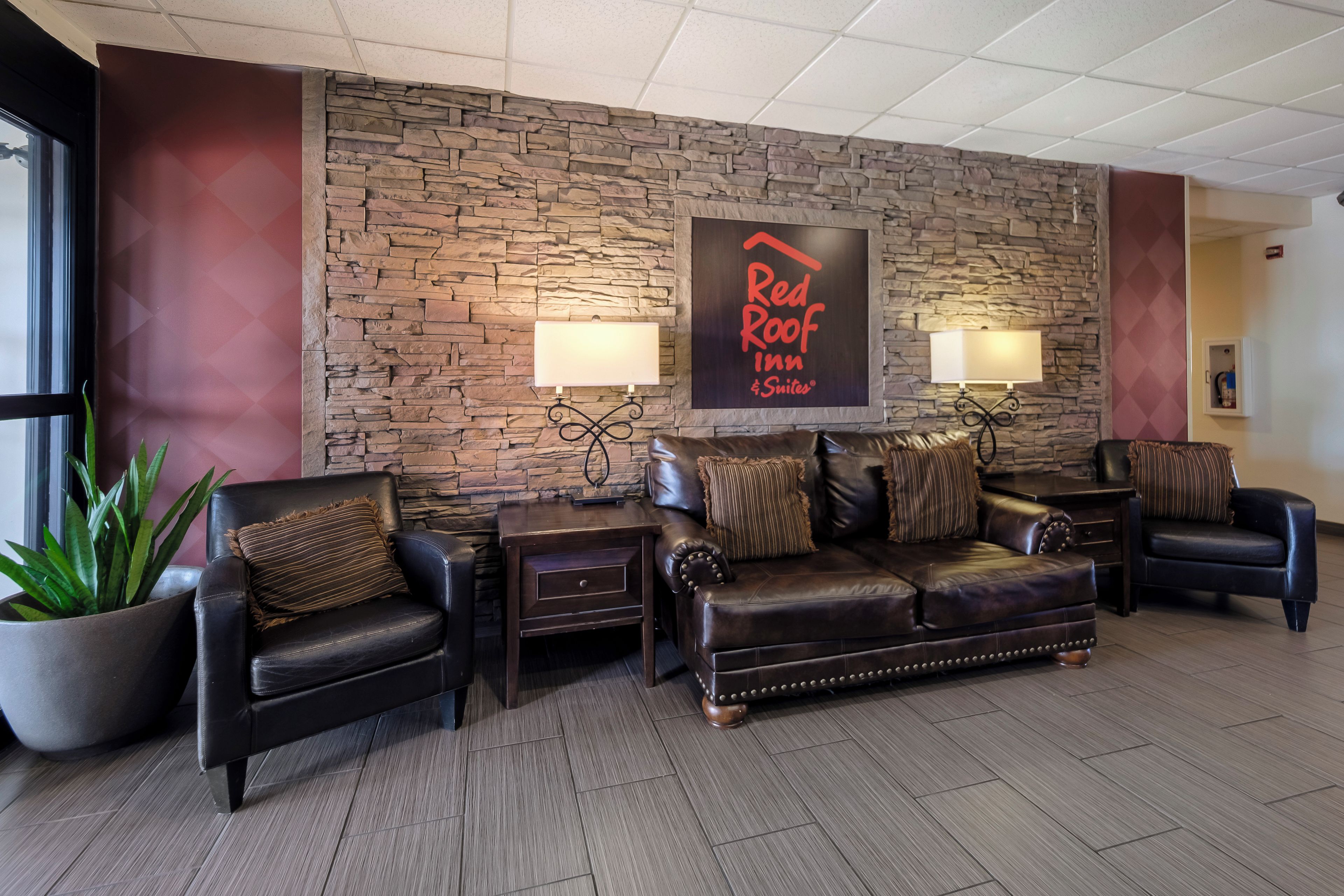 Lobby do Red Roof Inn & Suites com parede de pedra, sofás de couro, poltronas e uma grande planta em vaso.