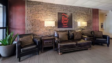 Lobby do Red Roof Inn & Suites com parede de pedra, sofás de couro, poltronas e uma grande planta em vaso.