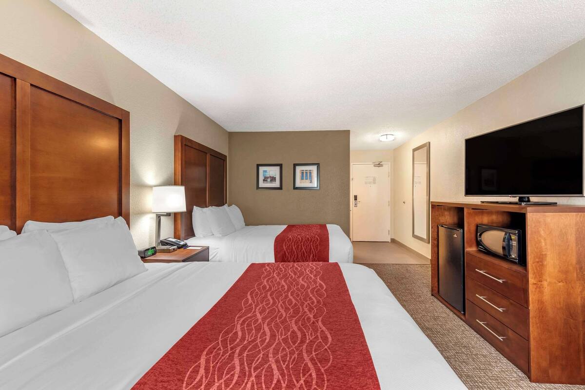 Quarto de hotel com duas camas, televisão, minibar e secretária com candeeiro.