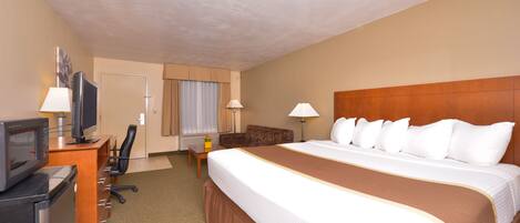 Quarto de hotel com uma cama grande, uma escrivaninha com televisão, uma cadeira e um abajur.