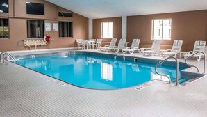 Piscina interna com água cristalina, rodeada por espreguiçadeiras brancas e piso em azulejo.