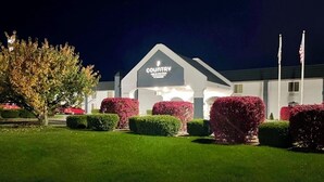 Um hotel Country Inn & Suites com fachada bem iluminada, cercado por sebes bem aparadas e uma grande árvore.