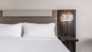 Quarto de hotel moderno com uma cama grande, cabeceira com painel luminoso geométrico e mesa de cabeceira com tomada.