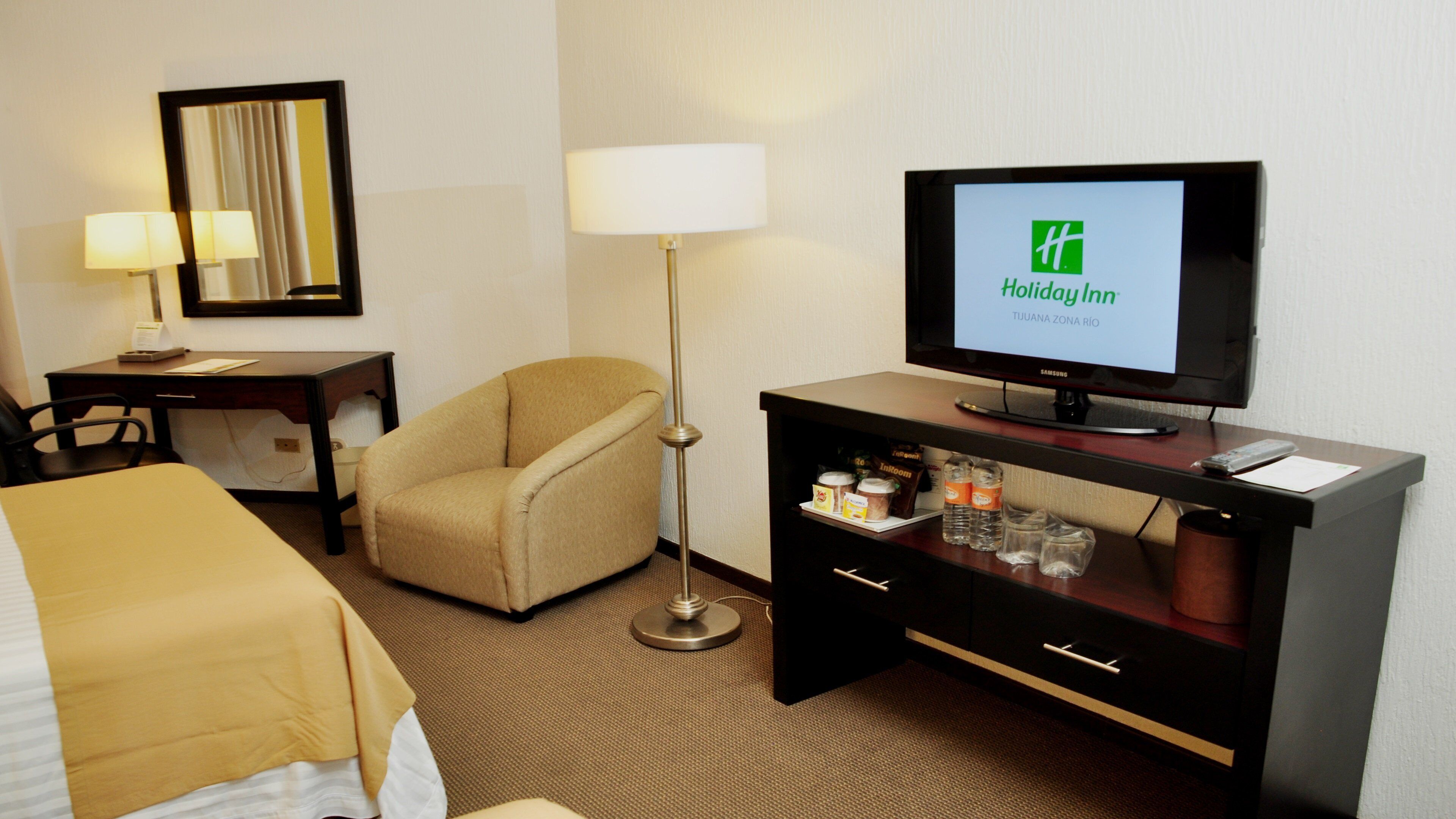 Quarto de hotel com cama, escrivaninha, cadeira, televisão e minibar.