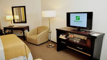 Quarto de hotel com cama, escrivaninha, cadeira, televisão e minibar.