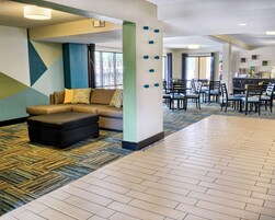 Um saguão de hotel com um sofá modular, um banquinho e uma área de jantar com cadeiras e mesas.