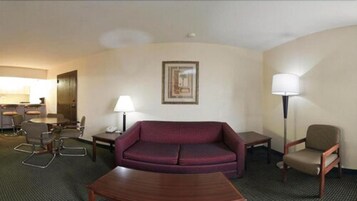 Quarto de hotel com sofá, poltronas, uma mesa pequena, abajur e um quadro na parede.