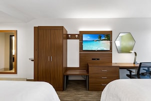 Quarto de hotel com escrivaninha de madeira, televisão, espelho e duas camas.