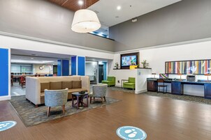 Uma área de lobby com sofá, cadeiras, uma mesa pequena, balcão de recepção e televisão.