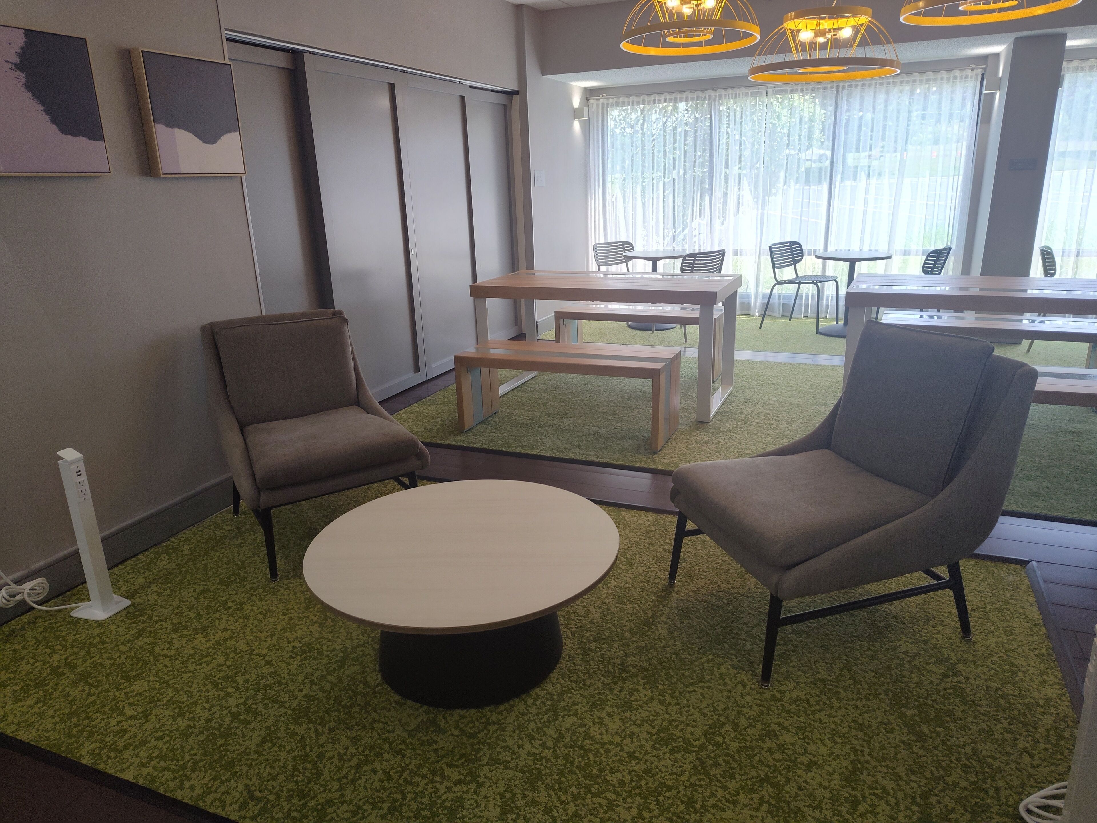 Uma sala de reuniões moderna com dois poltronas, uma mesa redonda e uma pequena mesa retangular.