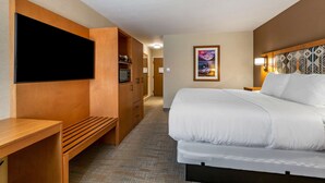 Quarto de hotel com uma cama grande, televisão de tela plana, móveis de madeira e um quadro na parede.