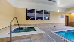 Piscina com banheira de hidromassagem, piso revestido e janela com vista.
