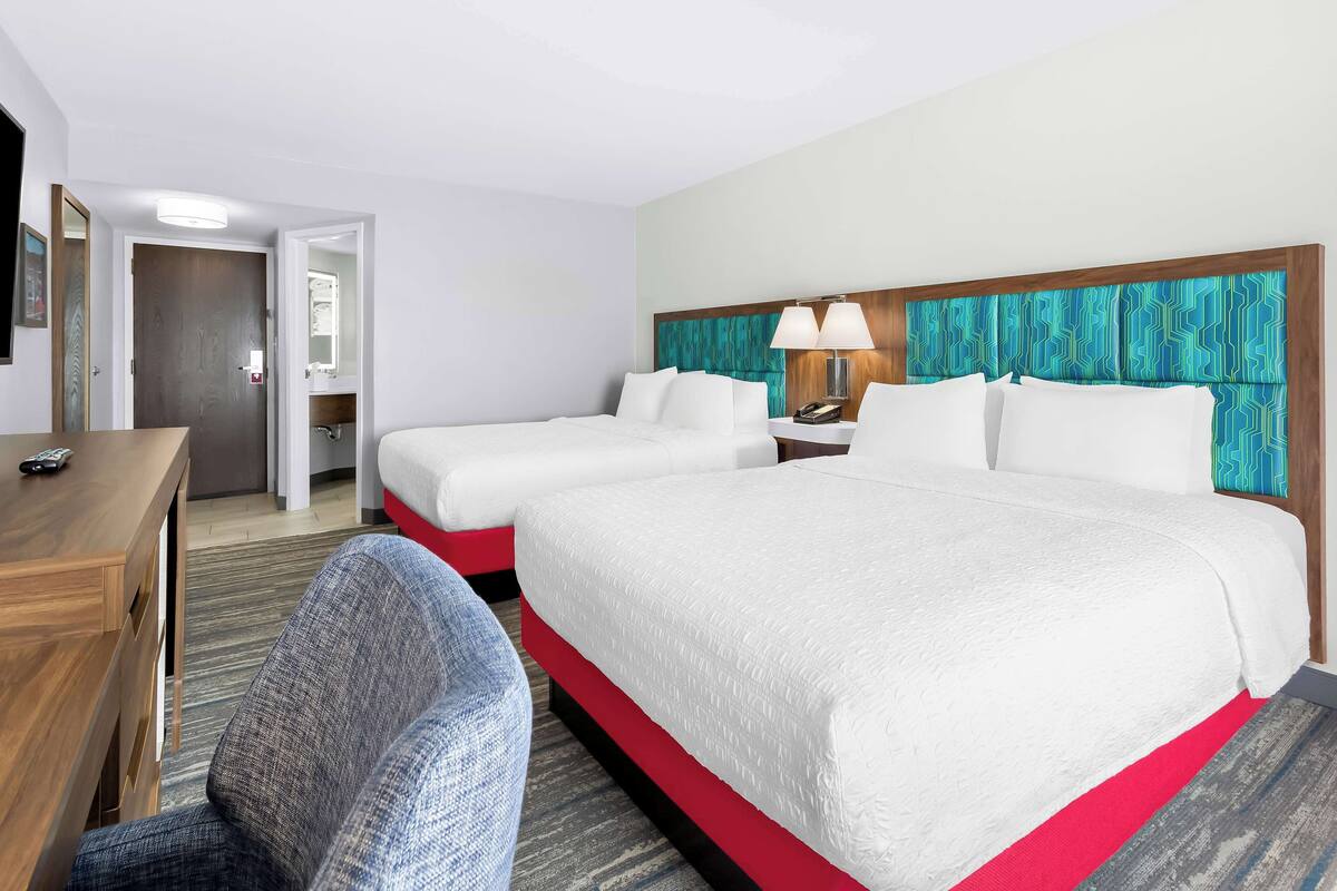 Quarto de hotel com duas camas, uma escrivaninha e uma cadeira.