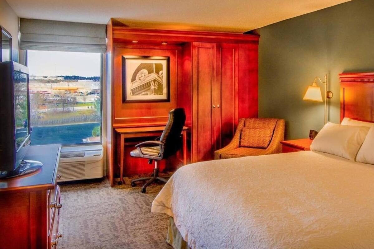 Quarto de hotel com cama, escrivaninha, cadeira, televisão e janela com vista.