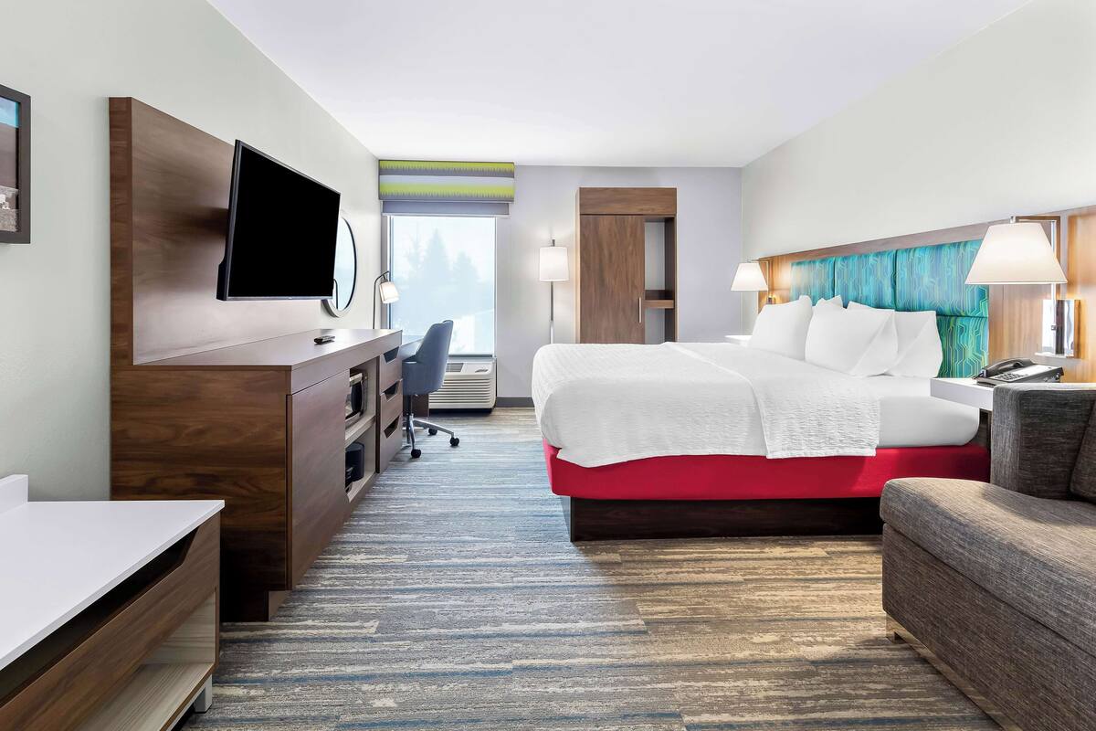 Quarto de hotel com cama, escrivaninha, cadeira, televisão e vista para o exterior.