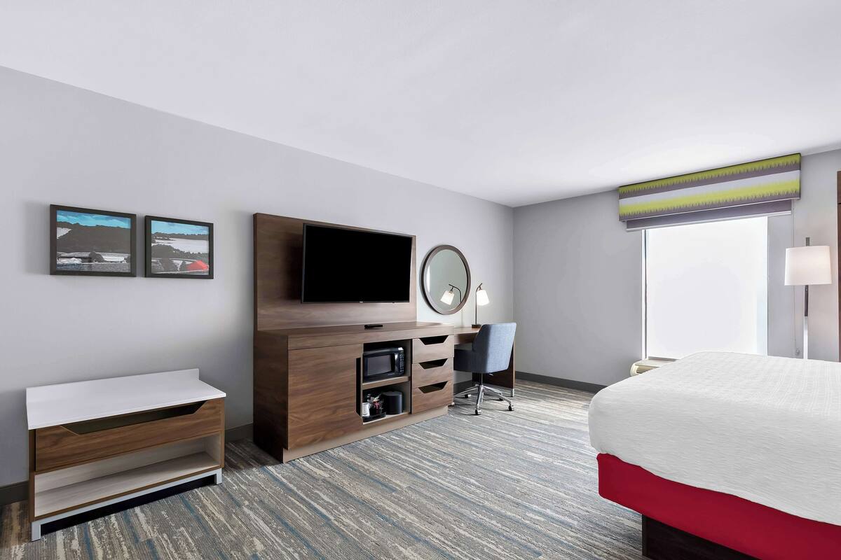 Quarto de hotel com uma cama, televisão, escrivaninha, cadeira e duas quadros na parede.