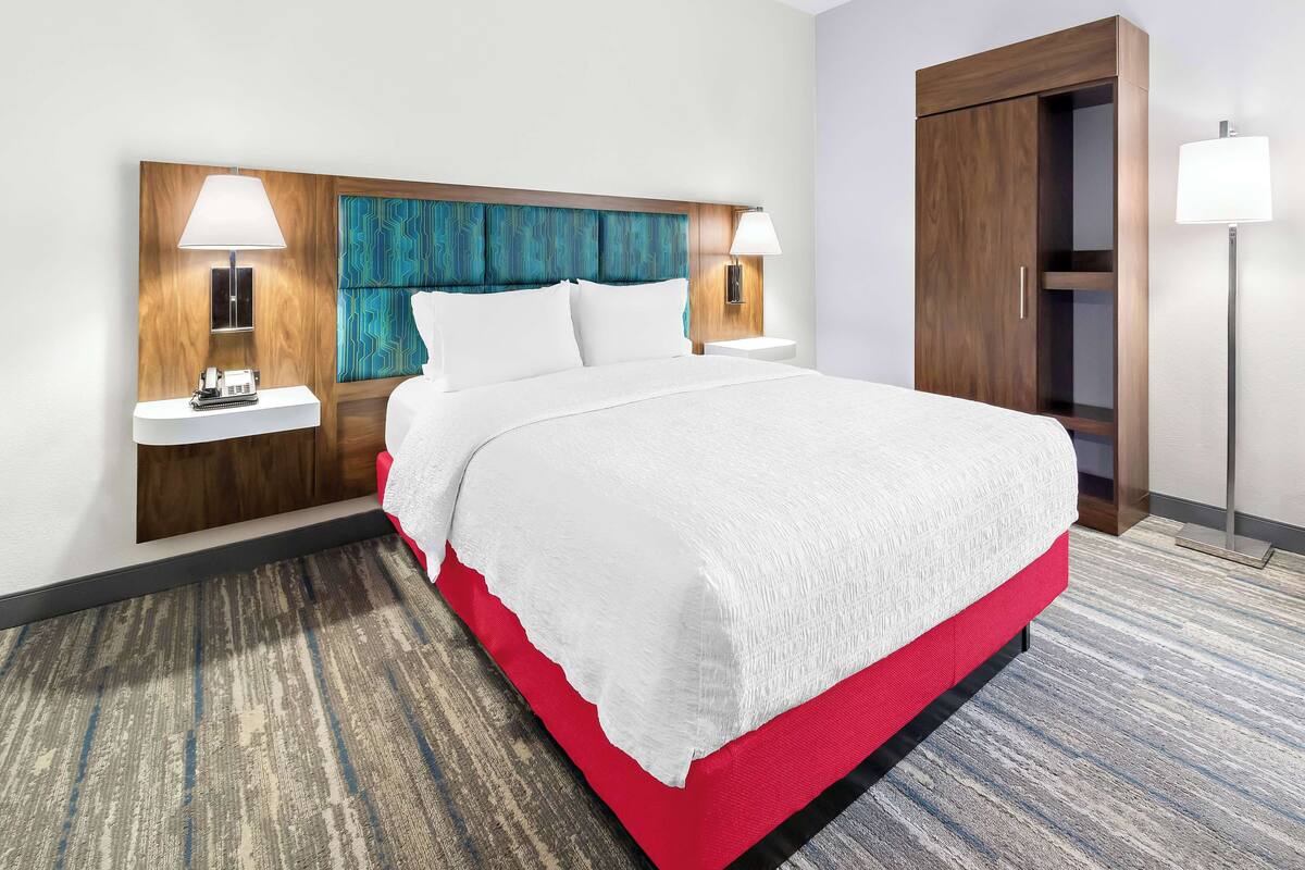 Quarto de hotel com uma cama grande, duas mesas de cabeceira com luminárias, um painel de cabeceira em madeira e um guarda-roupa.