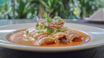Um prato de enchiladas com molho cremoso, coberto com abacate, rabanete e queijo, servido em um prato branco.