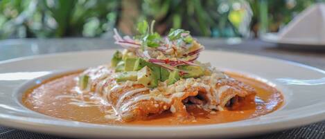 Um prato de enchiladas com molho cremoso, coberto com abacate, rabanete e queijo, servido em um prato branco.