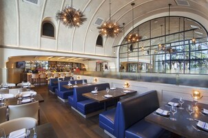 Um restaurante espaçoso com tetos altos, assentos azuis e uma grande janela com vista para o exterior.