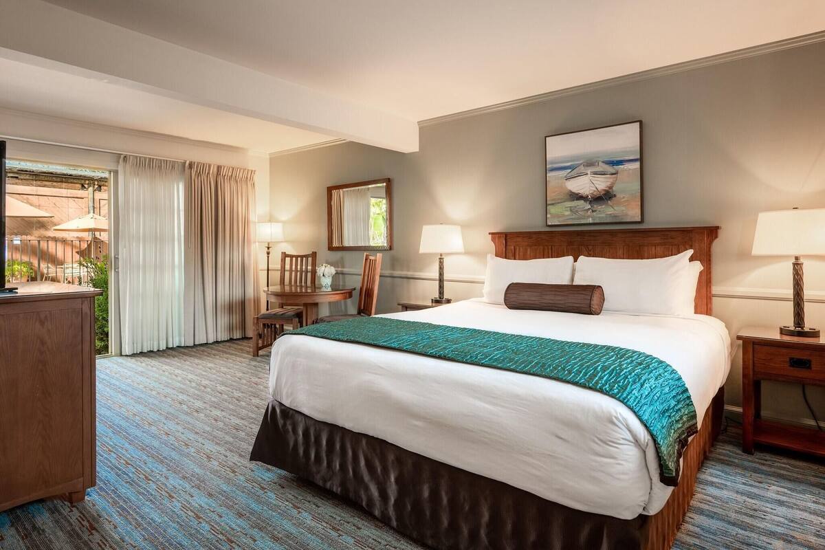 Quarto de hotel com uma cama grande, uma escrivaninha, uma cadeira e vista para o exterior.