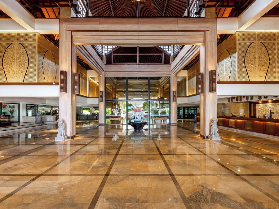 Um hall amplo com piso de mármore polido, uma fonte central e um balcão de recepção.