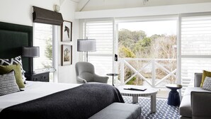 Quarto de hotel moderno com uma cama grande, área de estar com uma mesa e varanda com vista para árvores.