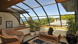 Quarto aconchegante com um amplo claraboia, mobiliário de vime, plantas em vasos e vista para a paisagem.