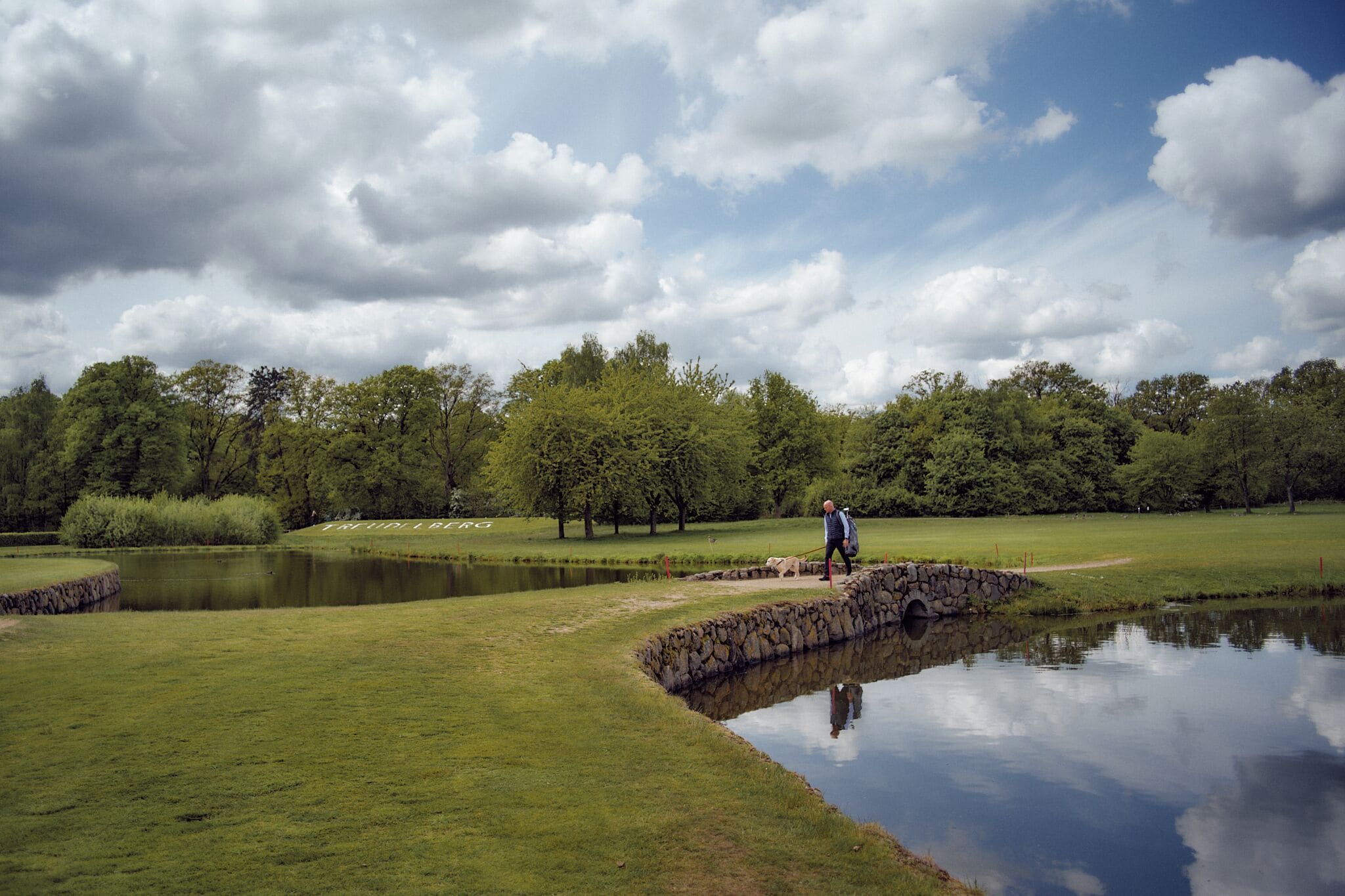 Um campo de golfe tranquilo com lago, ponte de pedra e vegetação exuberante.
