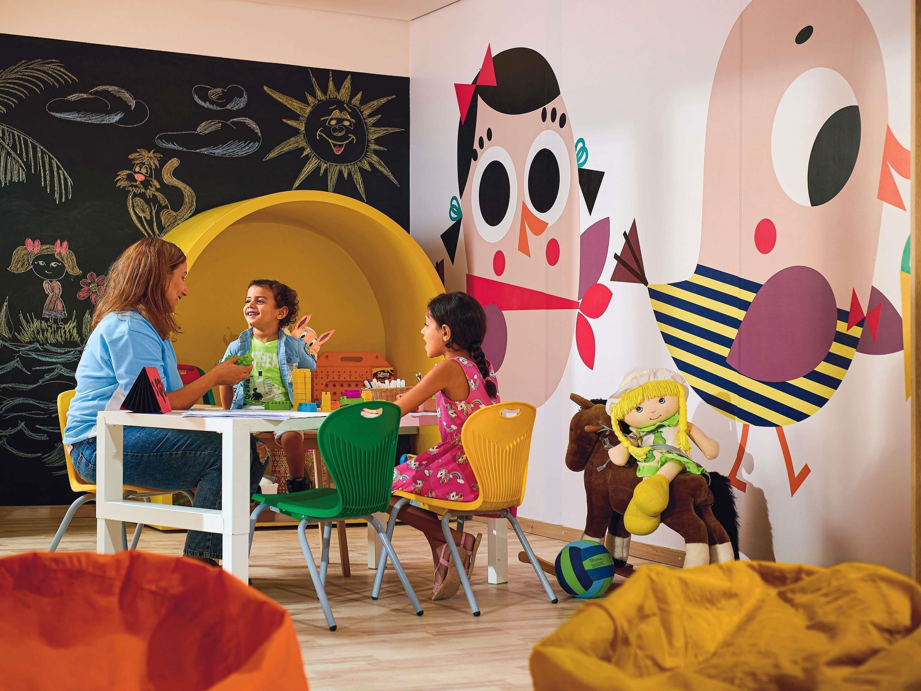 Um quarto com uma mesa branca, cadeiras coloridas e um mural com personagens de desenho animado.