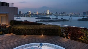 Banheira de hidromassagem com pétalas de rosas em deck de madeira com vista para a paisagem urbana e uma ponte.