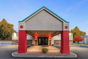 Um edifício com fachada bege, detalhes em vermelho e telhado verde.