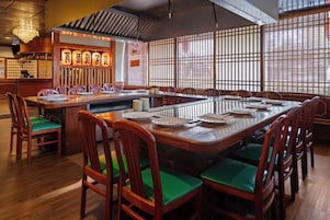 Um restaurante com decoração tradicional japonesa, apresentando mesas e cadeiras de madeira, um balcão de sushi e portas deslizantes.
