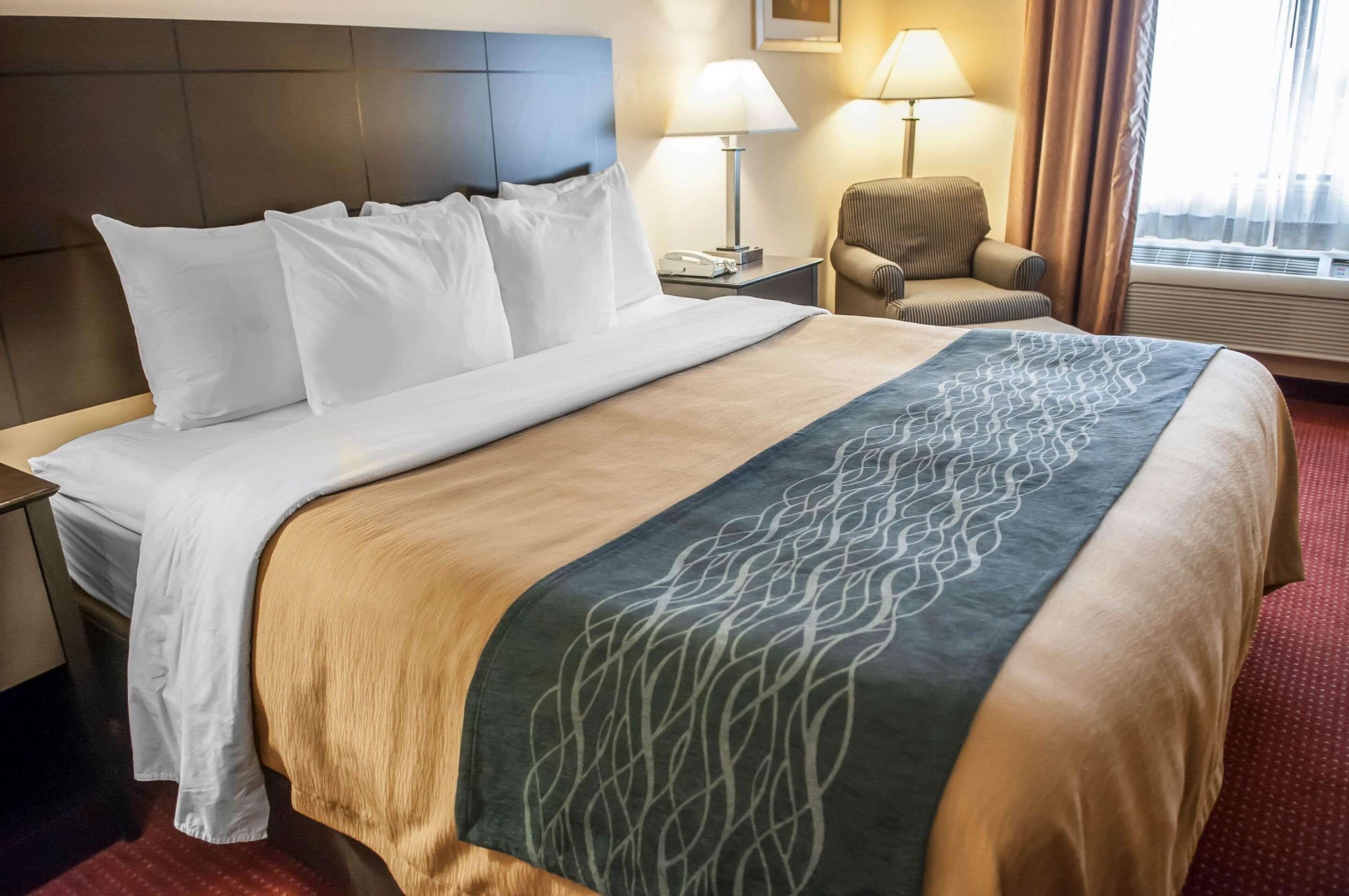 Quarto de hotel com uma cama grande, duas luminárias de cabeceira, uma cadeira e vista para a cidade pela janela.