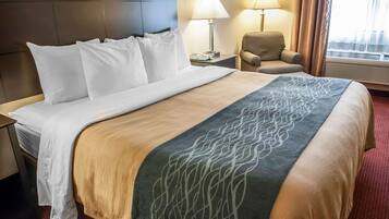 Quarto de hotel com uma cama grande, duas luminárias de cabeceira, uma cadeira e vista para a cidade pela janela.