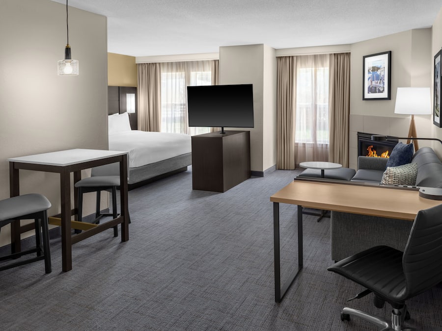 Quarto de hotel com cama, escrivaninha com cadeira, televisão, lareira e sofá.