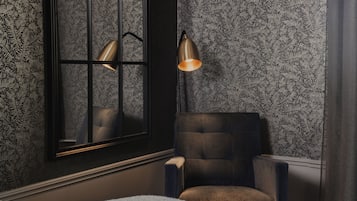 Quarto de canto com poltrona escura, janela com moldura preta e papel de parede estampado.