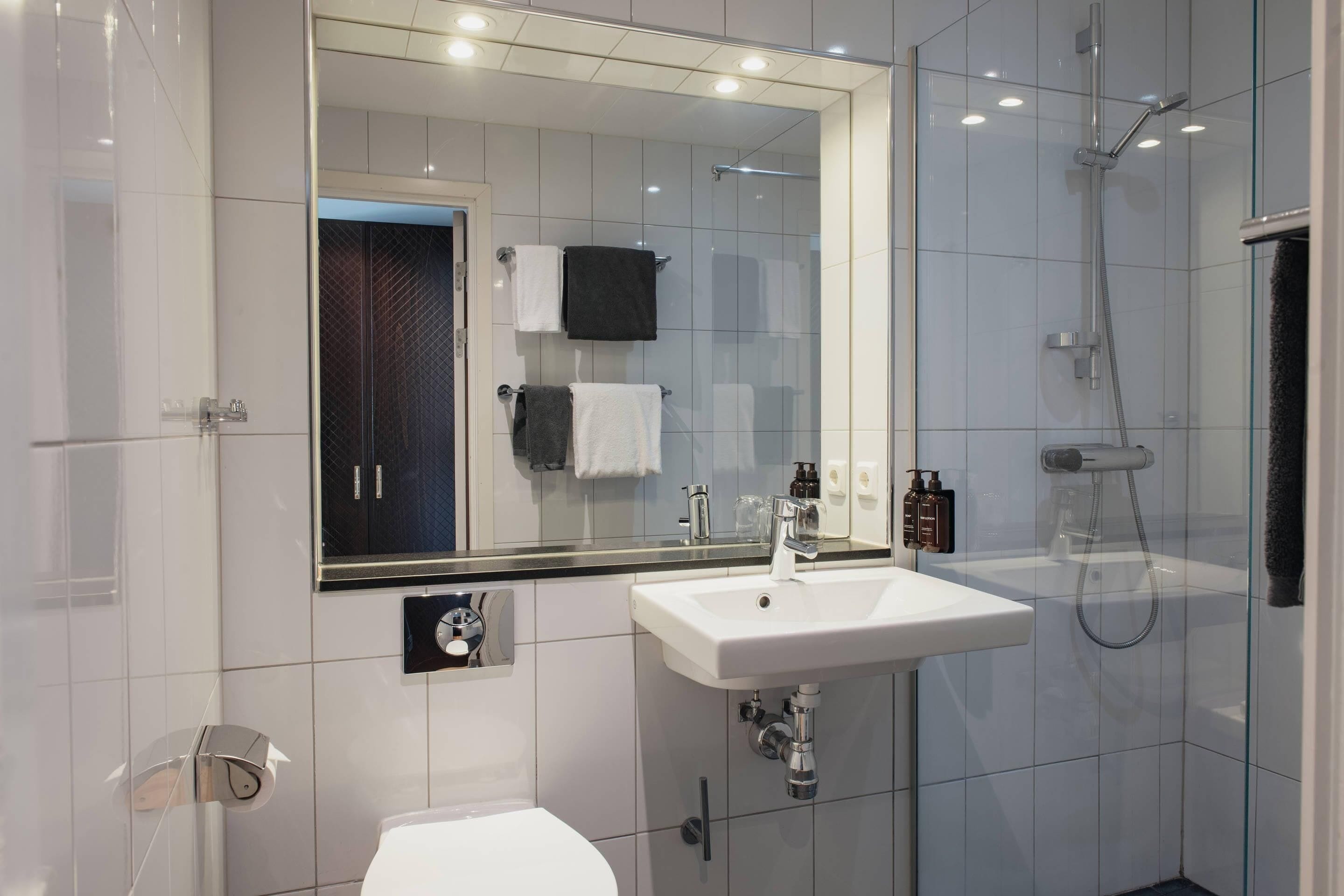 Uma casa de banho moderna com uma sanita branca, um espelho e uma cabine de duche com portas de vidro.