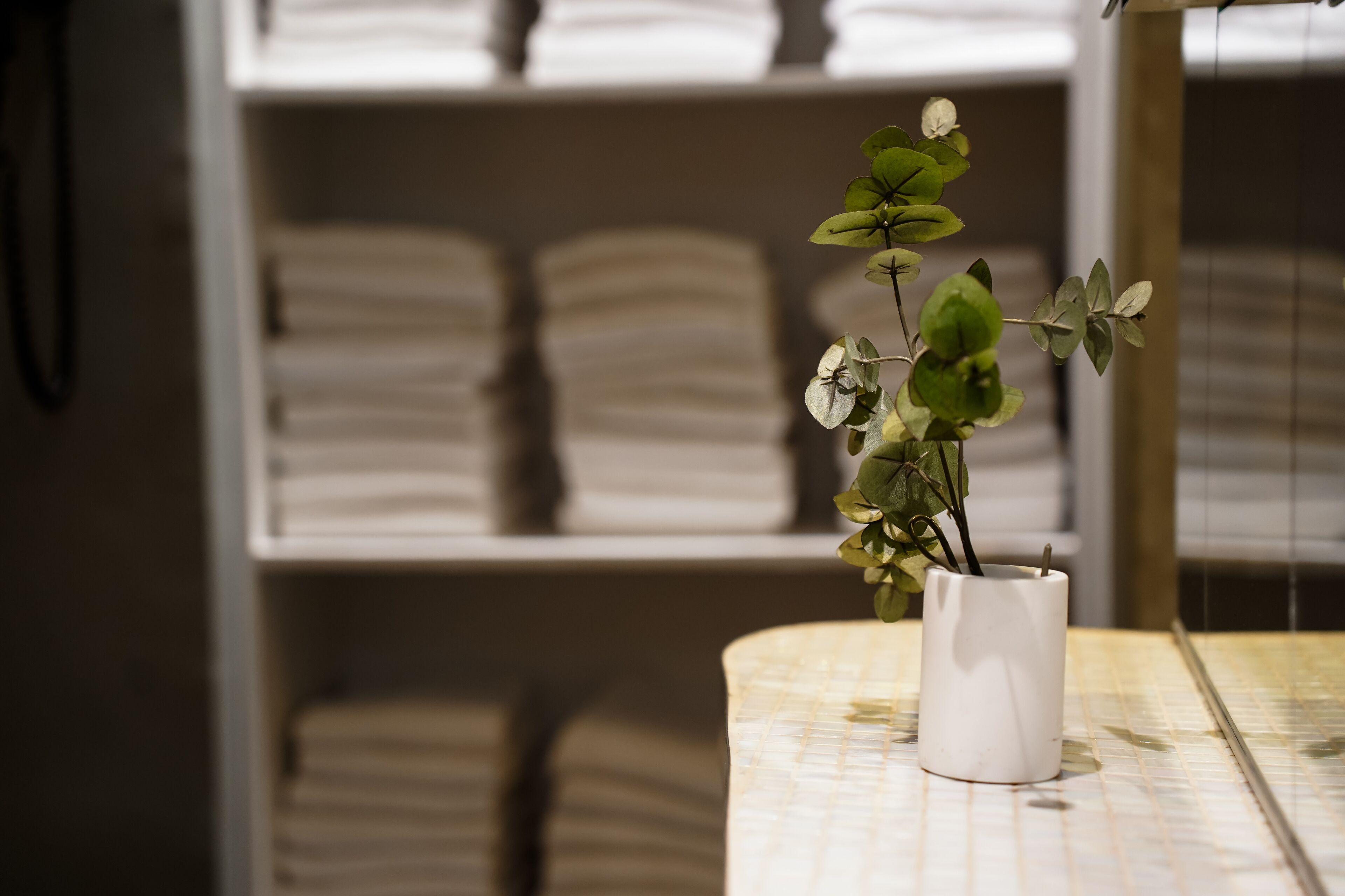 Vaso branco com folhas verdes sobre um piso de azulejos.