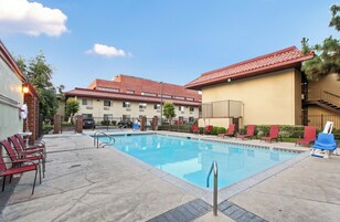 Piscina com espreguiçadeiras e um edifício com telhado de telhas vermelhas ao fundo.