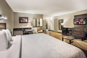 Quarto de hotel com cama grande, escrivaninha, cadeira, televisão e guarda-roupa.