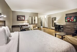 Quarto de hotel com cama grande, escrivaninha, cadeira, televisão e guarda-roupa.