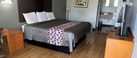 Quarto de hotel com cama, escrivaninha, cômoda, espelho, quadro emoldurado e televisão.