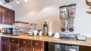 Uma área de cozinha com cafeteira, dispensadores de cereais, micro-ondas e frigorífico.