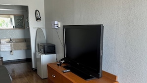 Quarto de hotel com cômoda de madeira, televisão de tela plana, micro-ondas, mini-geladeira, pia e espelho.